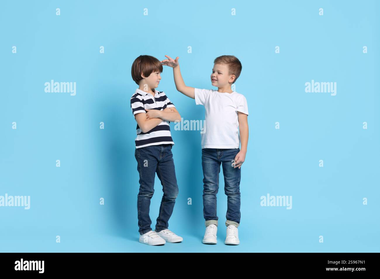 Cute brothers comparing their height on light blue background Stock ...