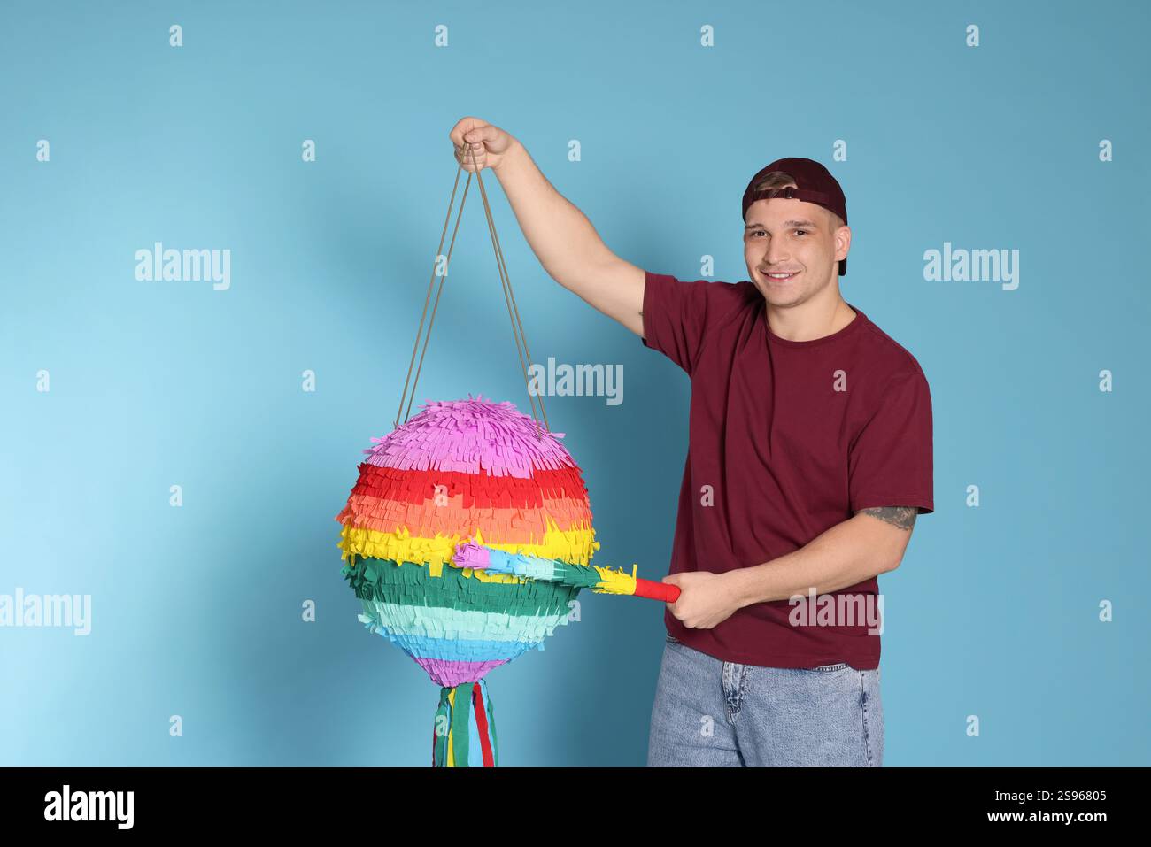 Happy man breaking pinata on light blue background Stock Photo - Alamy