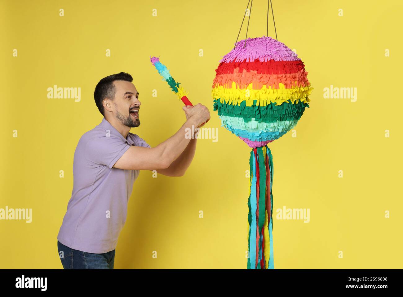 Emotional man hitting colorful pinata with stick on yellow background ...