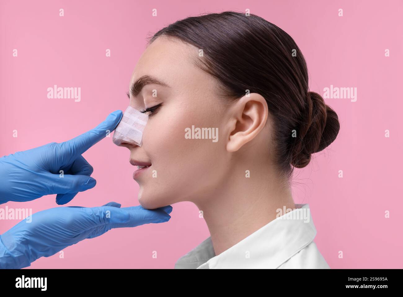 Doctor checking patient's nose after plastic surgery operation on pink ...