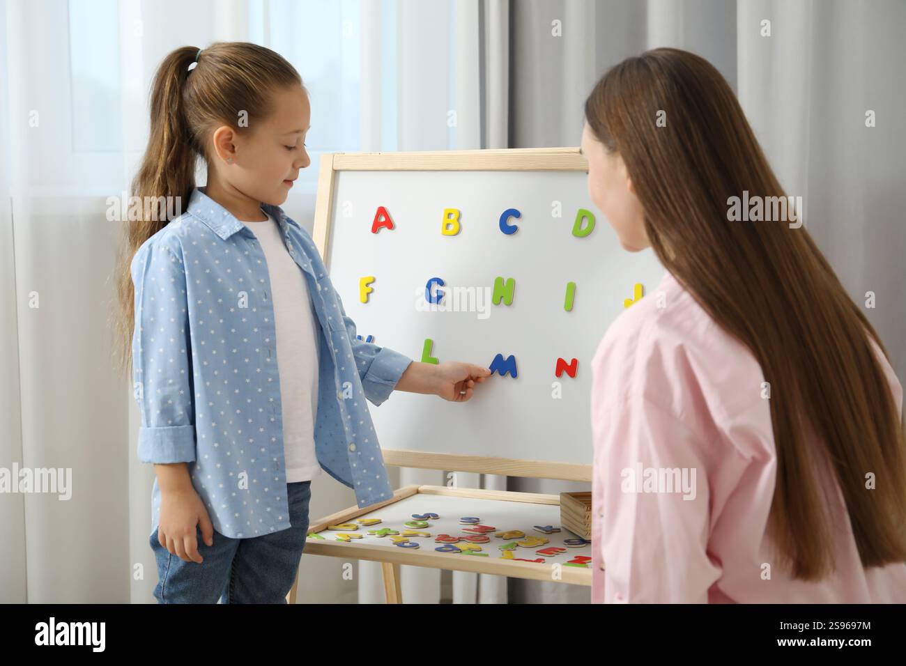 Speech therapist teaching little girl alphabet with magnetic letters ...