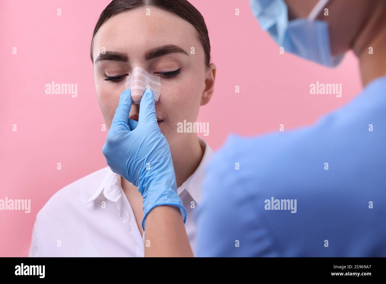 Doctor checking patient's nose after plastic surgery operation on pink ...