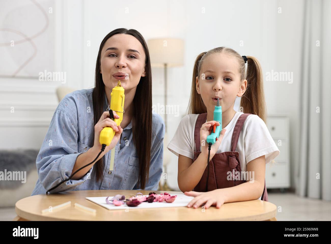 Family portrait of mother and daughter with hot glue guns at table ...