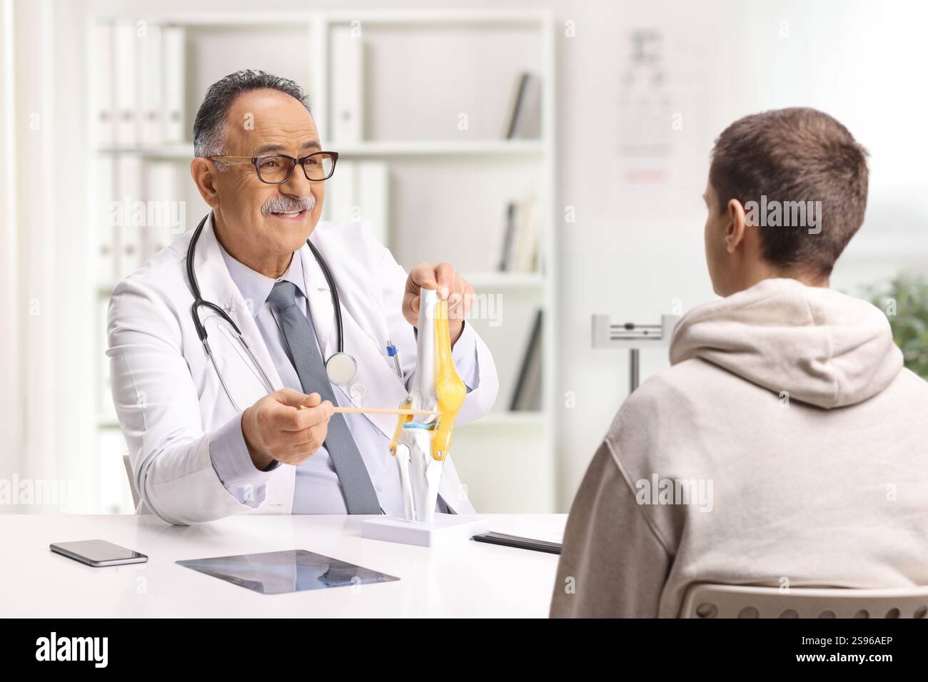 Orthopedic doctor explaining a knee bone model to a young male patient ...