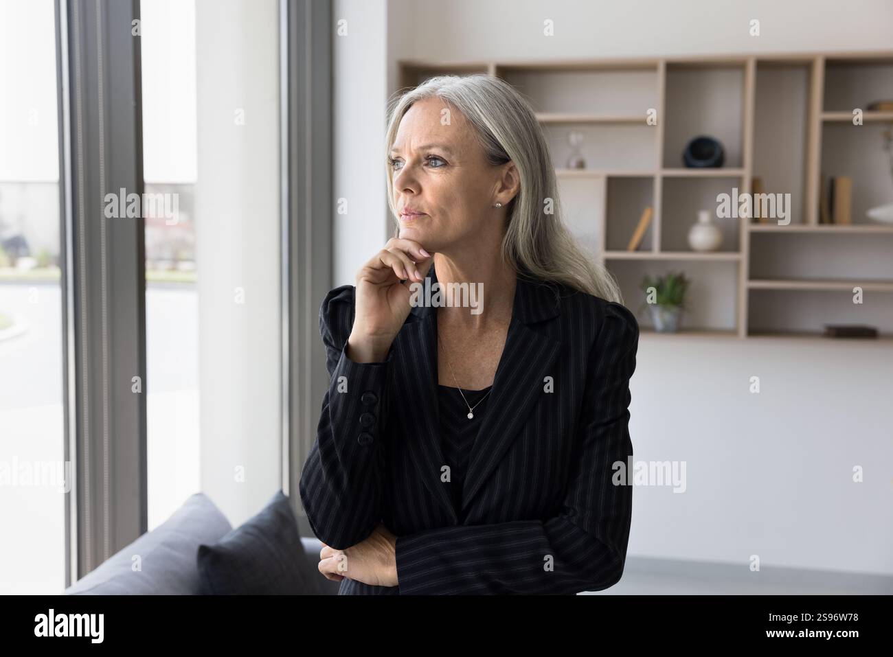 Professional 50s businesswoman looking out window with pensive ...