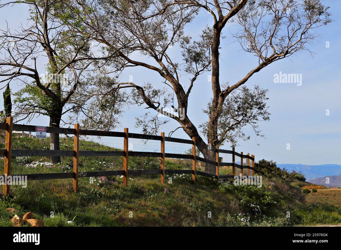 A wooden fence runs along a hillside of an estate with trees in the ...