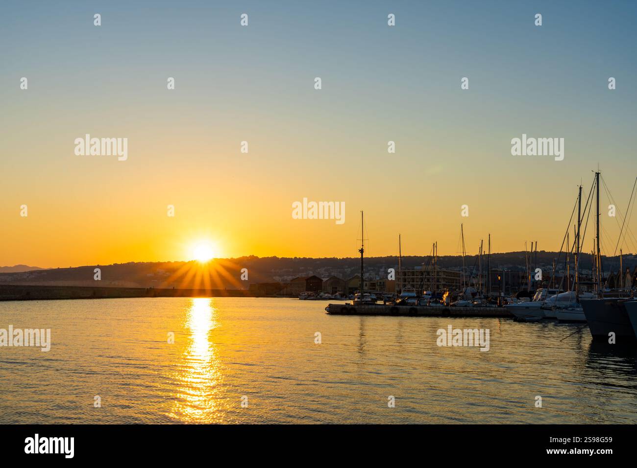 Sun sets across the bay at Chania and shadows over buildings and boats ...