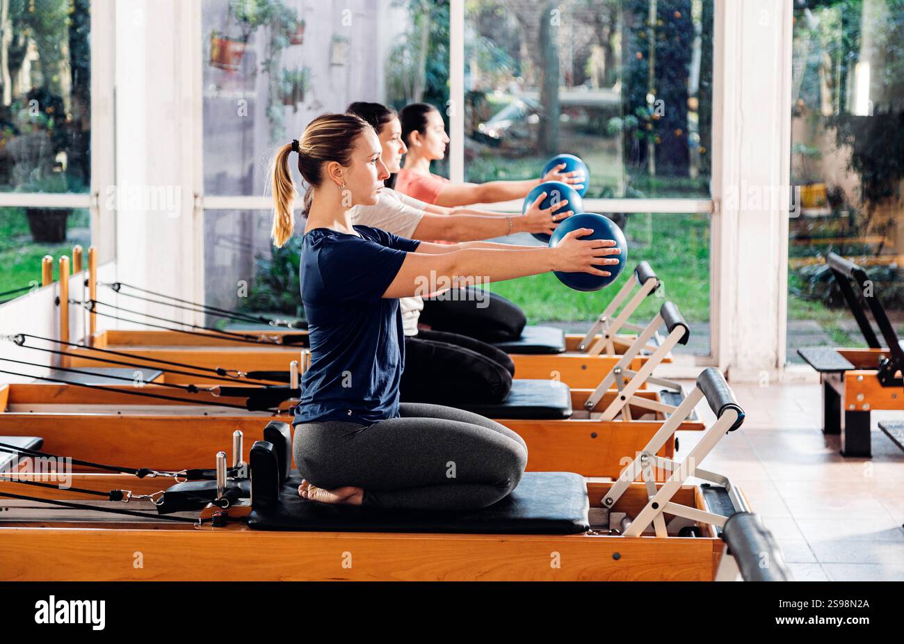 Three young, fit women training pilates with balls on a reformer bed ...