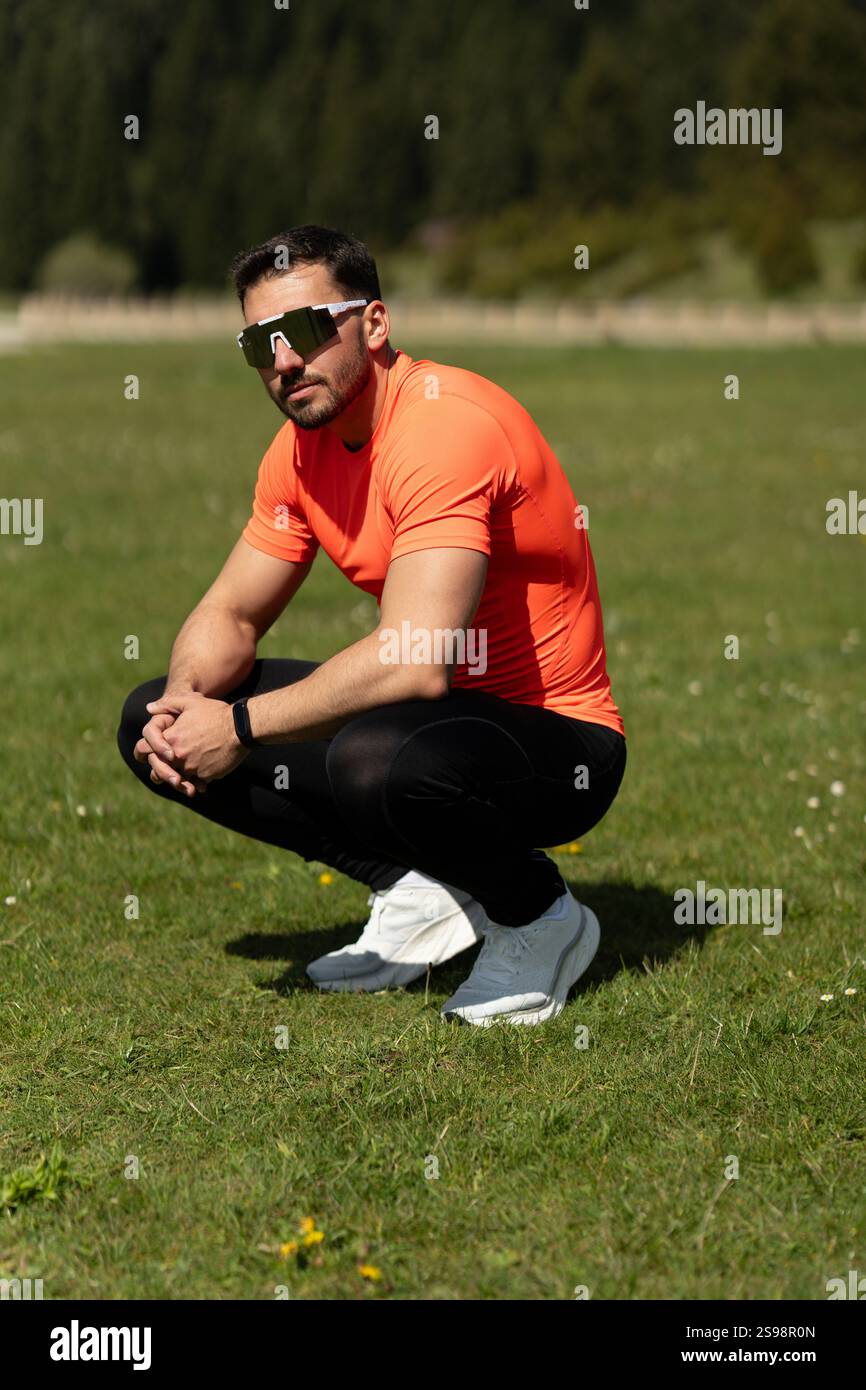 Male Fitness Enthusiast Takes A Break Squatting On Grass In A Tranquil ...