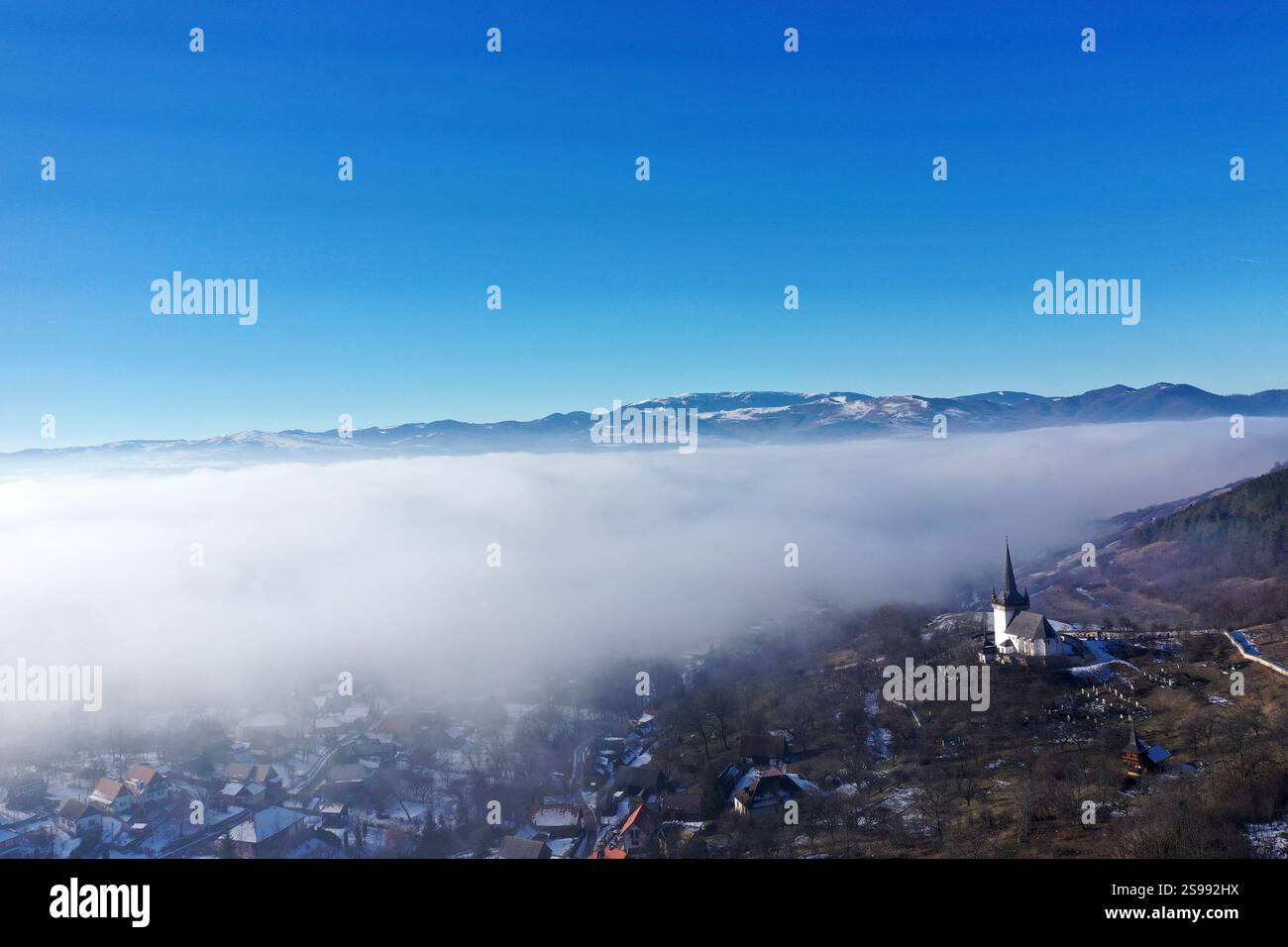 Aerial view of foggy misty mountain village and church tower at winter ...