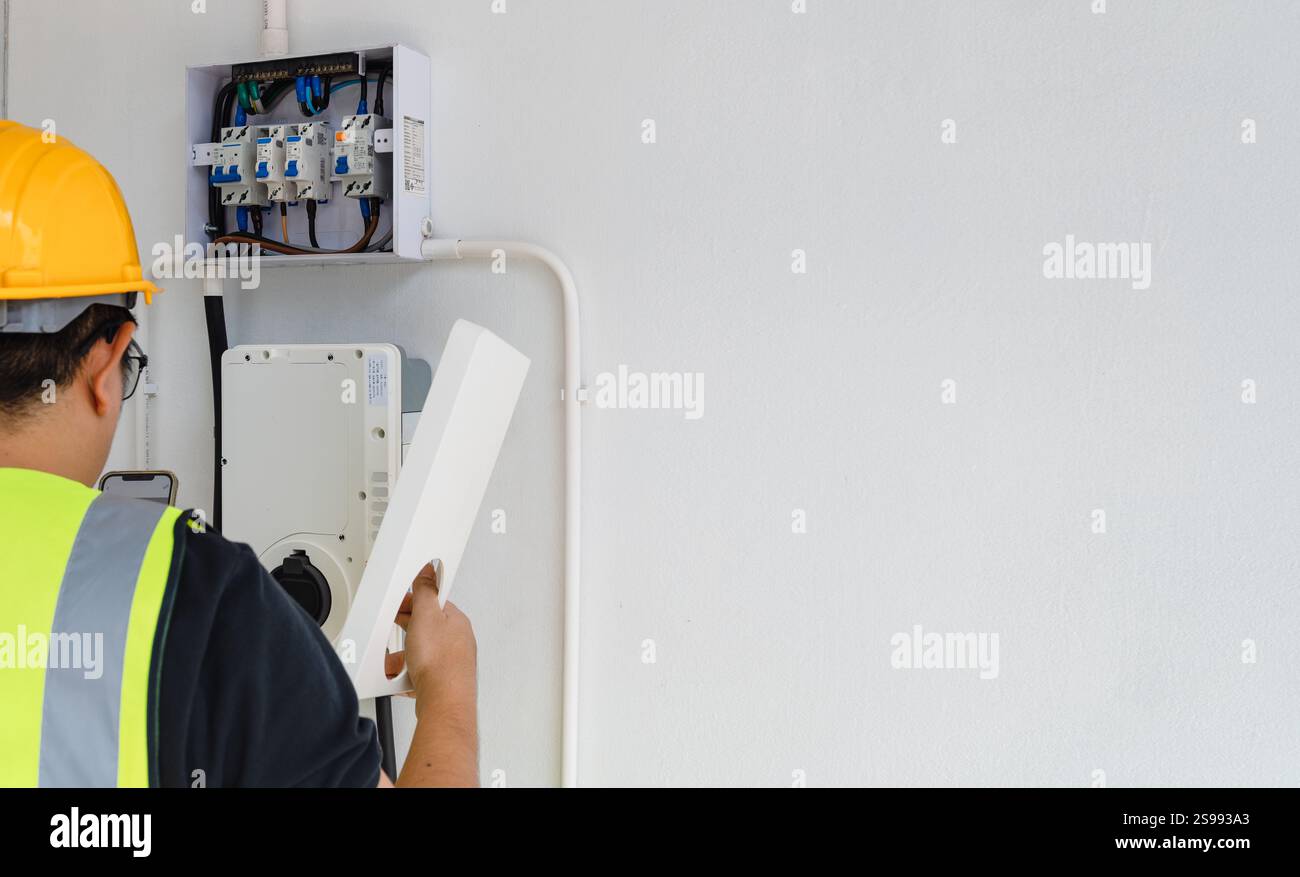 Technician wearing a yellow hard hat installing an electric vehicle ...