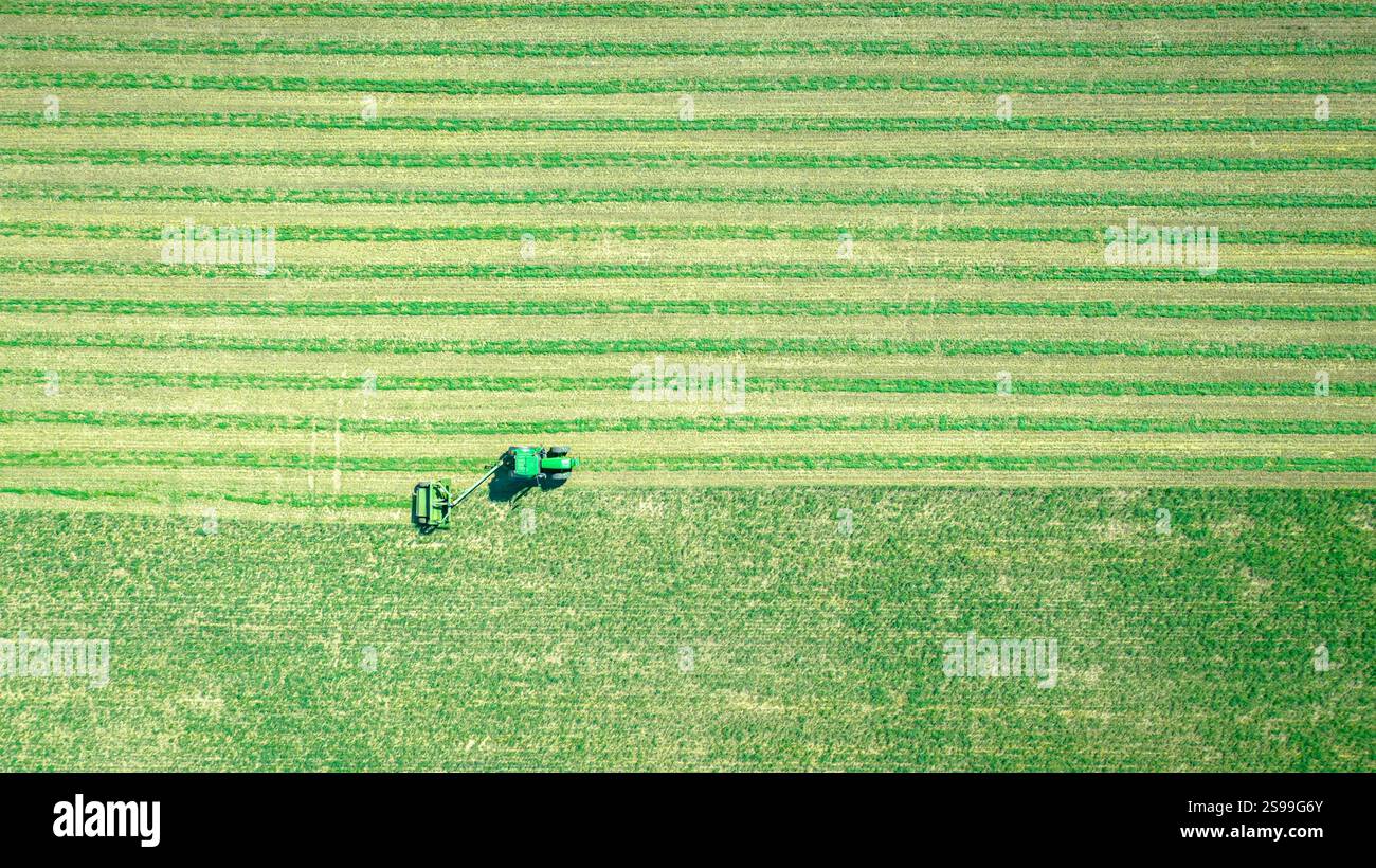 Above top view, tractor is pulling grass cutting machine over field ...