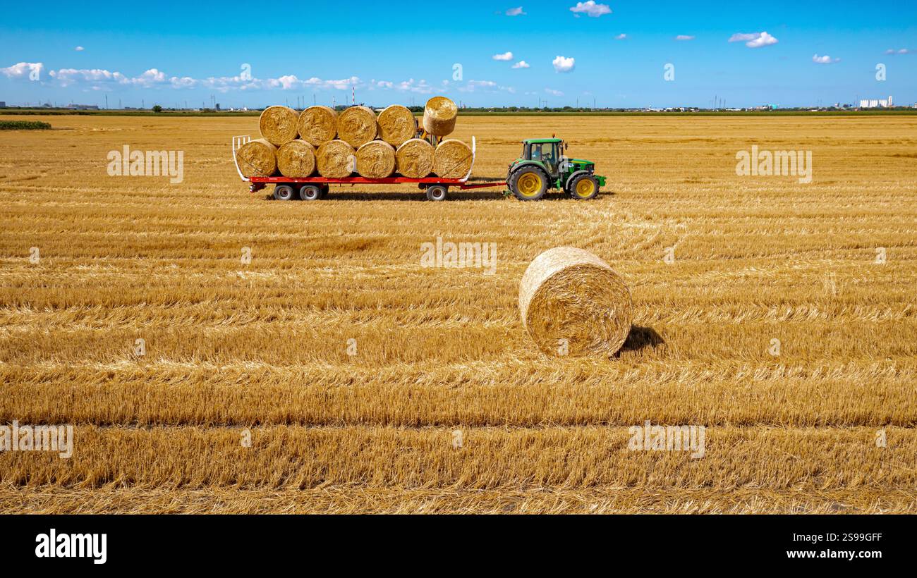 Above lateral view on excavator as loading straw bales on trailer, tow ...