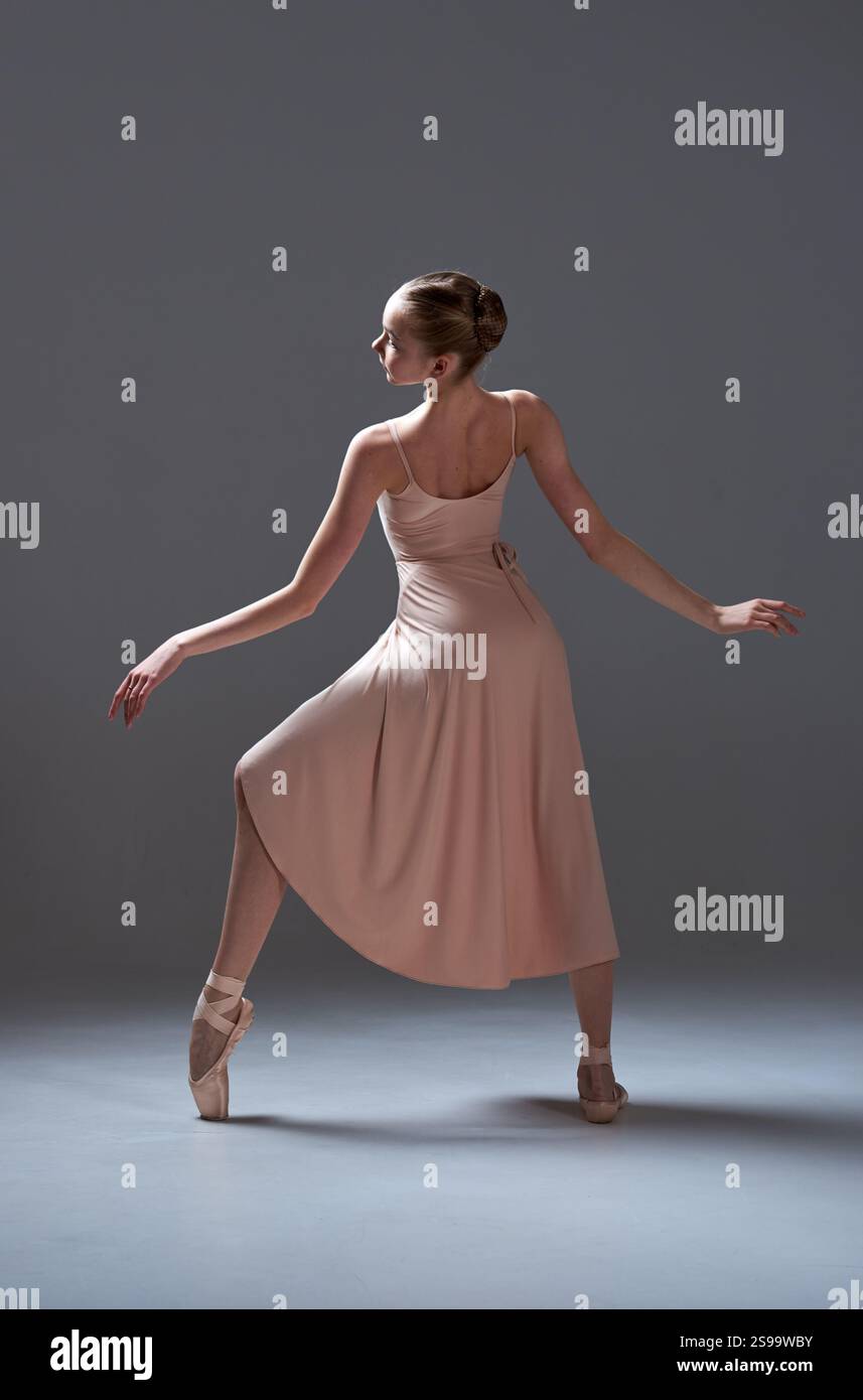 Ballet dancer in elegant peach dress shows classical pose on pointe shoes in a minimalist gray ...