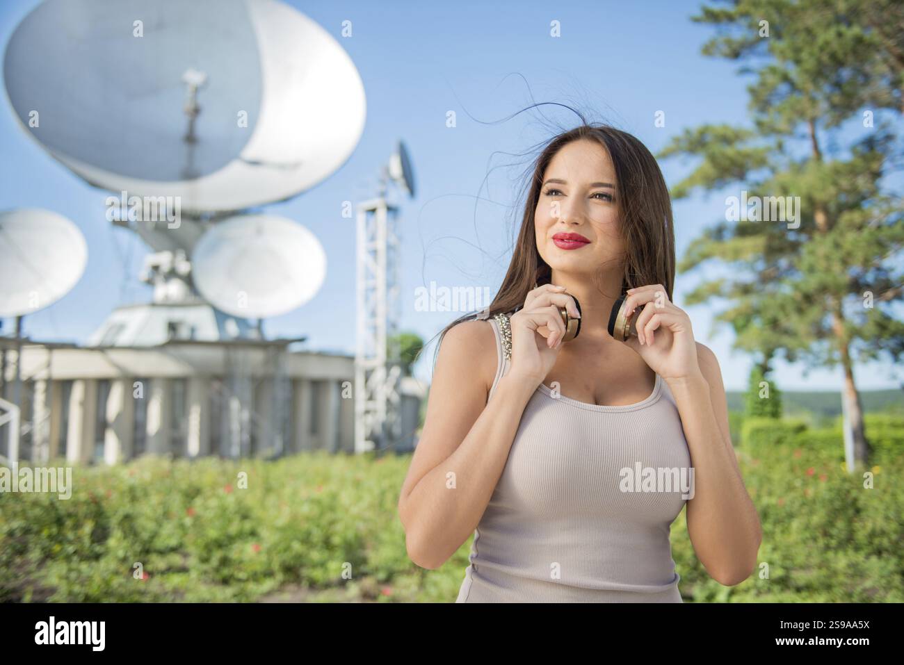 Beautiful young woman wearing headphones around her neck and standing ...