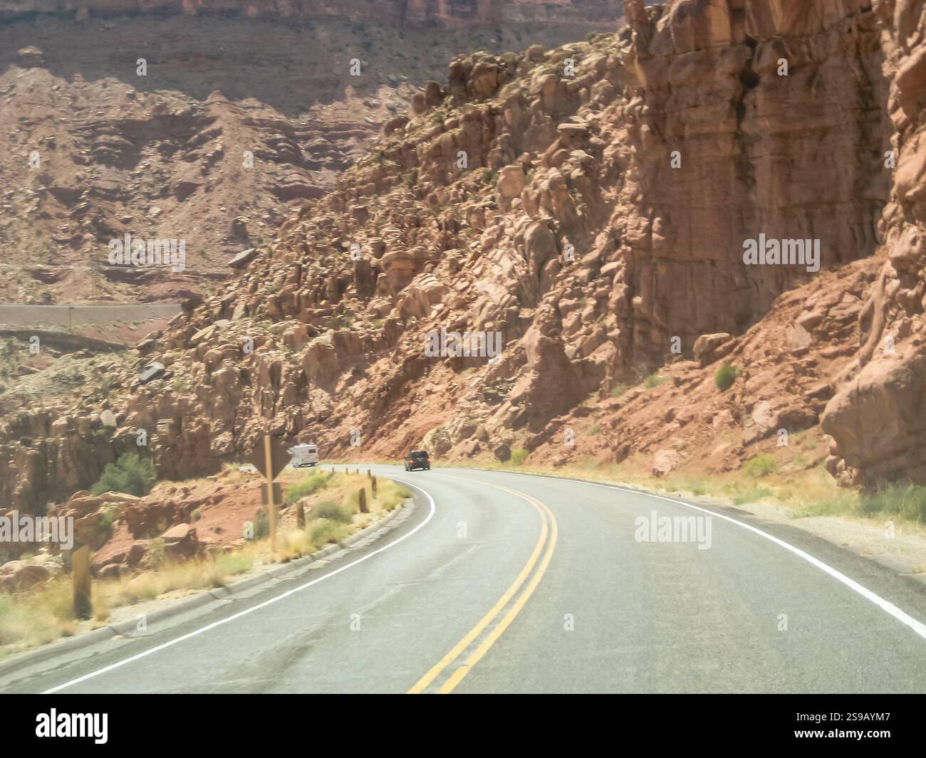 A road with a car driving down it. The road is lined with rocks and the ...