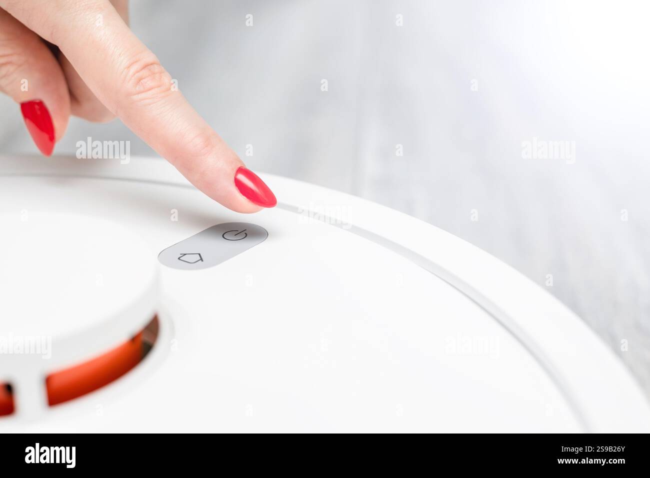 a woman's finger presses the power button of a robot vacuum cleaner ...