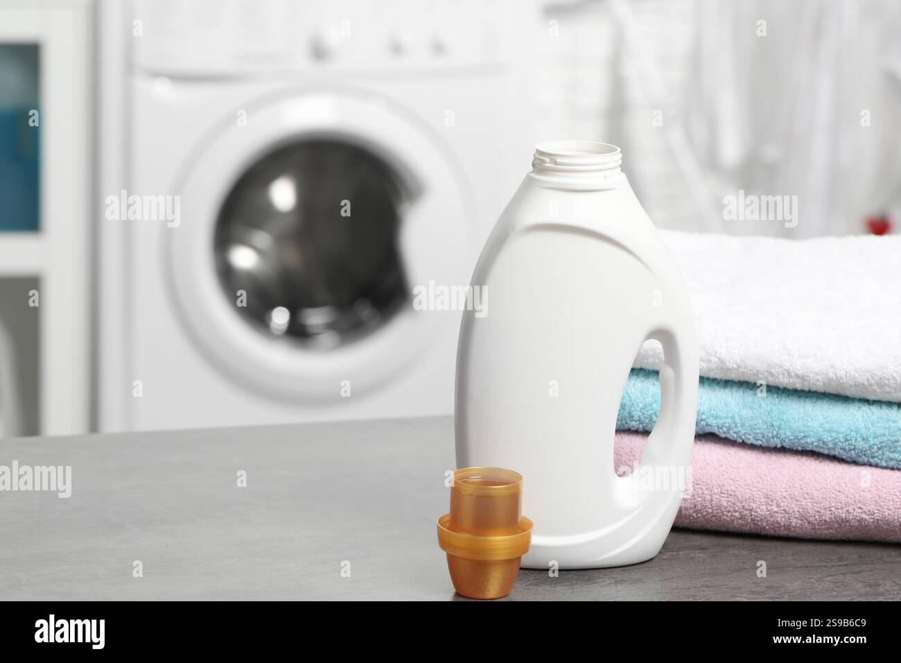 Laundry detergent, cap and stacked clean towels on grey table, space ...