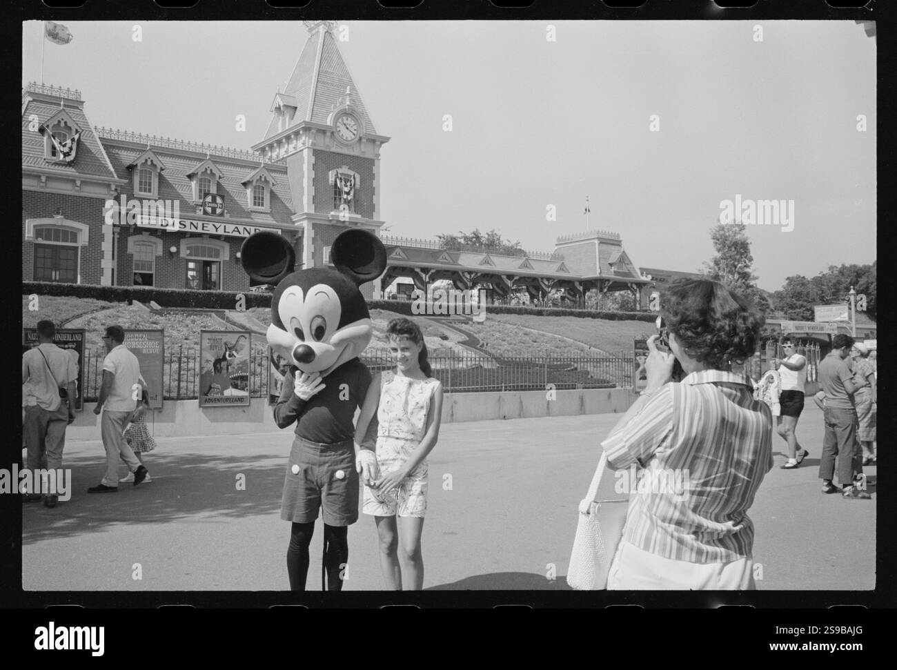 Woman (right, back to camera) taking a photograph of a girl posing with ...