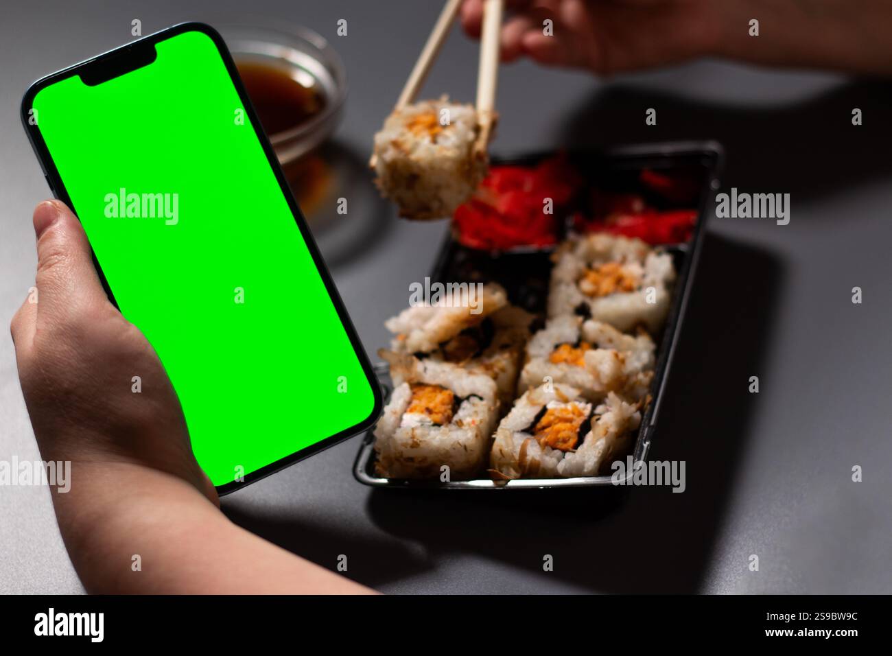 Female using smartphone while eating sushi rolls at home. Smartphone ...
