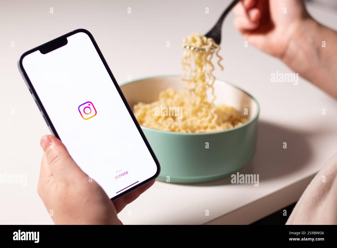 Female using instagram app on smartphone while eating pasta at home. Instagram logo on screen ...