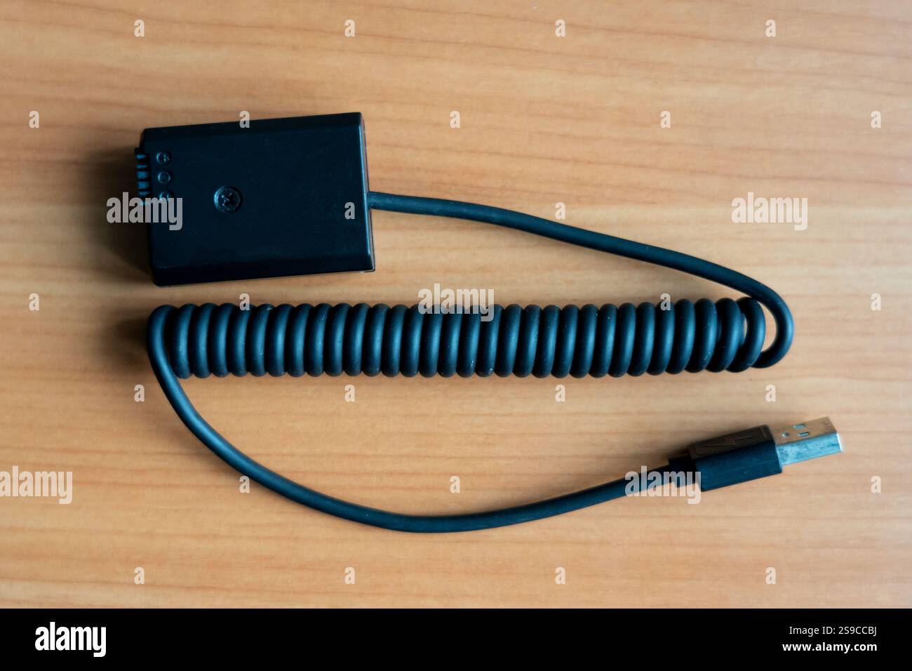 A coiled USB cable connector rests on a wooden surface. It features a ...