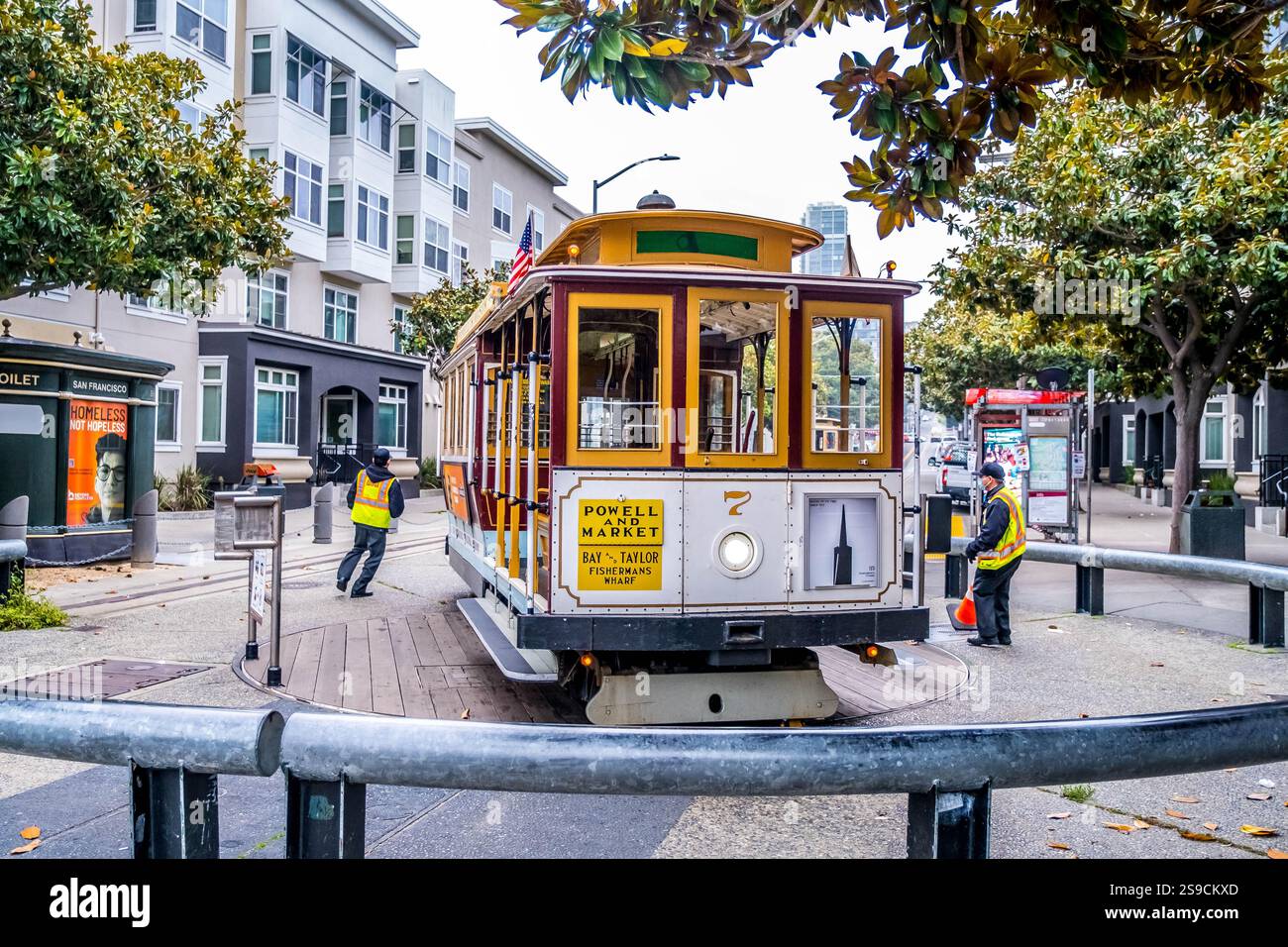 A vintage cable car makes a turn at Powell Market, surrounded by modern ...