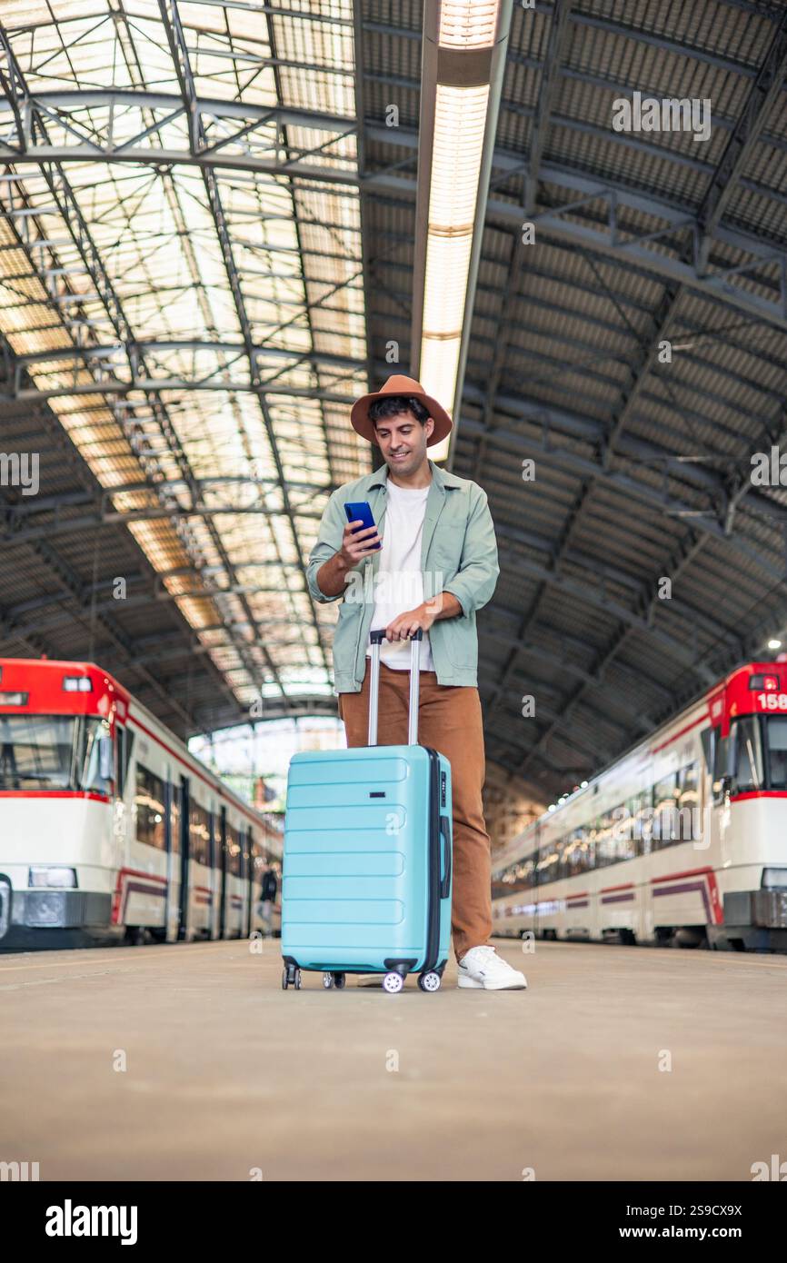 vertical Young latin male tourist wearing a hat and pulling a trolley ...