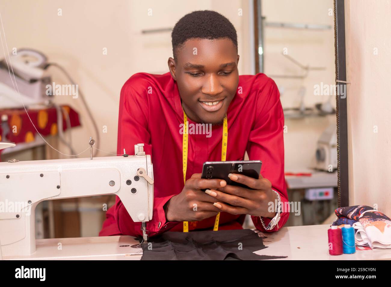 An African tailor using his phone while working in his workshop ...