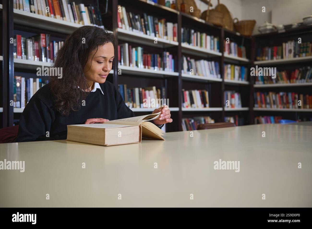 A thoughtful woman sits at a desk in a library surrounded by ...