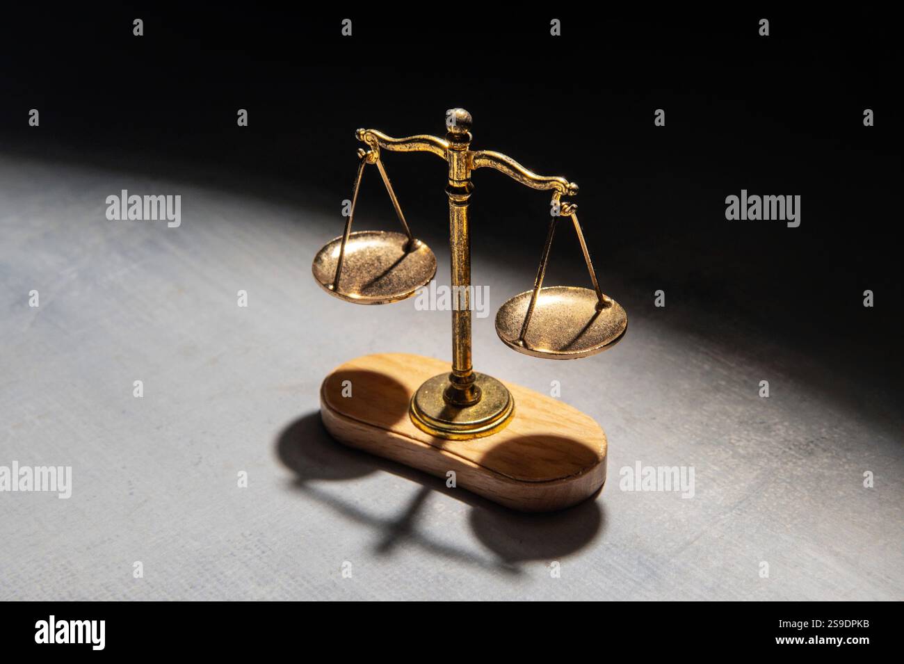 A scale of justice illuminated by a spotlight stands against a dark ...