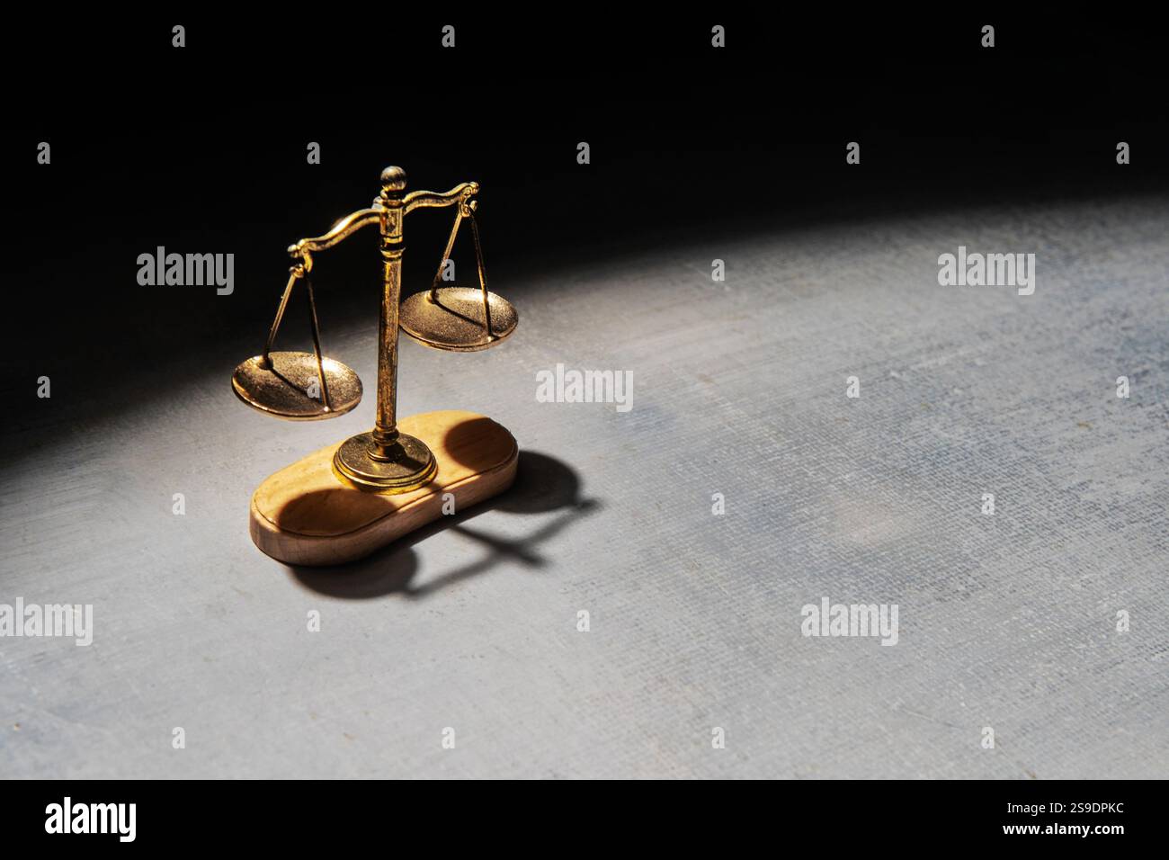 A scale of justice illuminated by a spotlight stands against a dark background, symbolizing ...