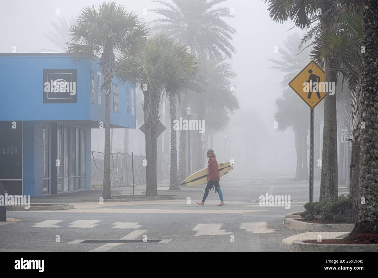 A surfer makes his way toward the beach in the early morning fog at ...