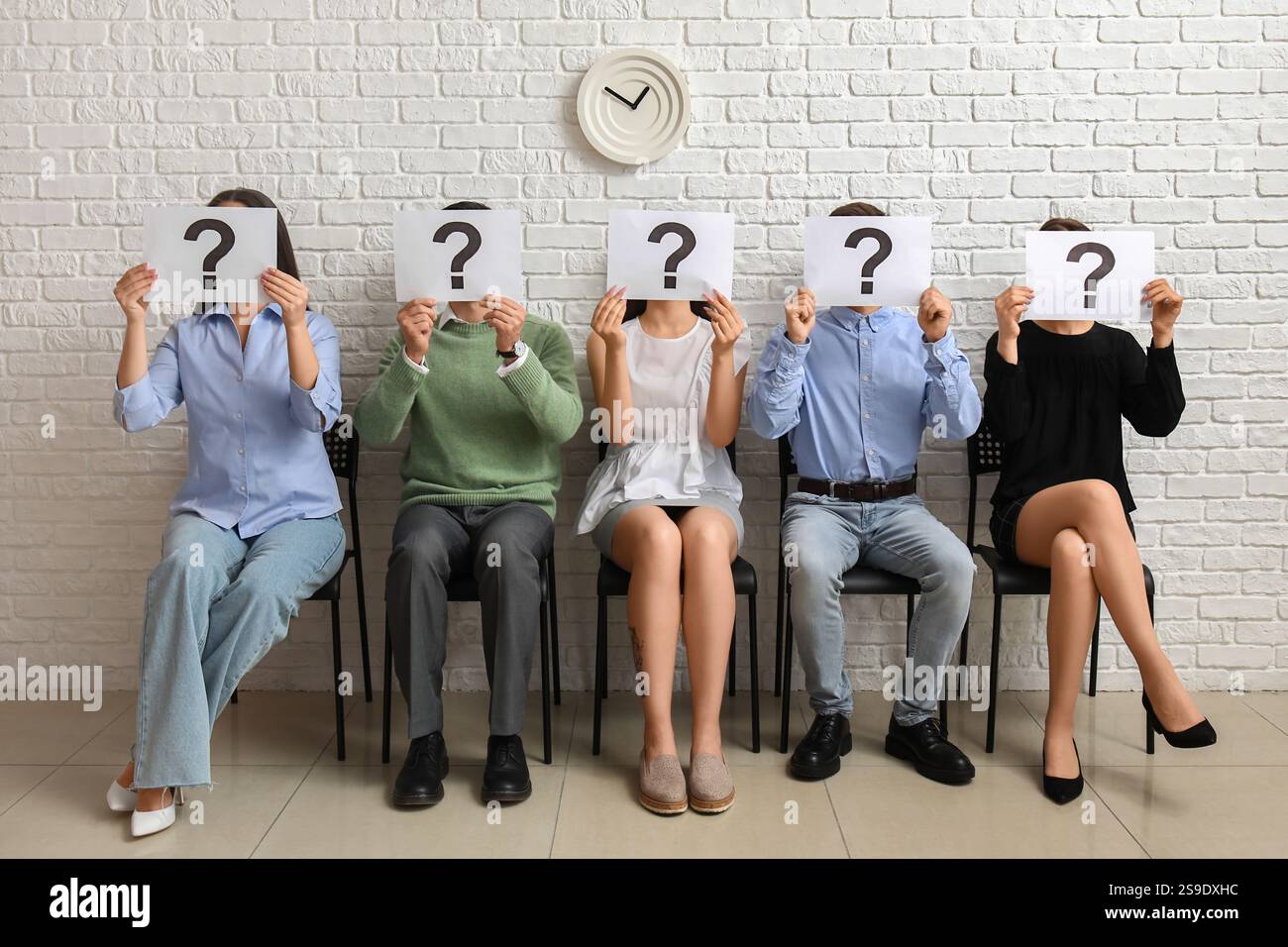 Young people holding paper sheets with question marks while waiting for ...