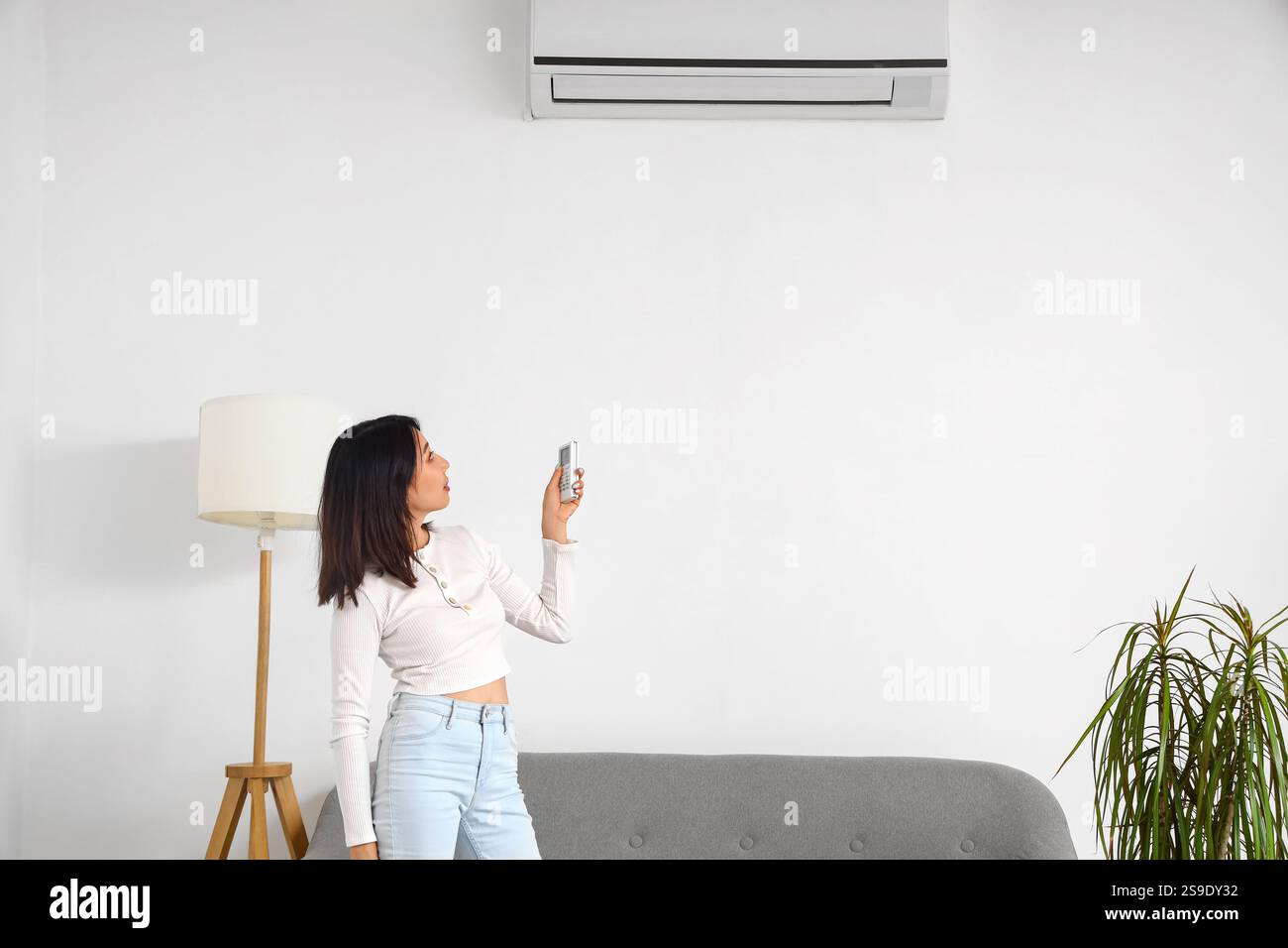 Beautiful Asian woman switching on air conditioner at home Stock Photo - Alamy