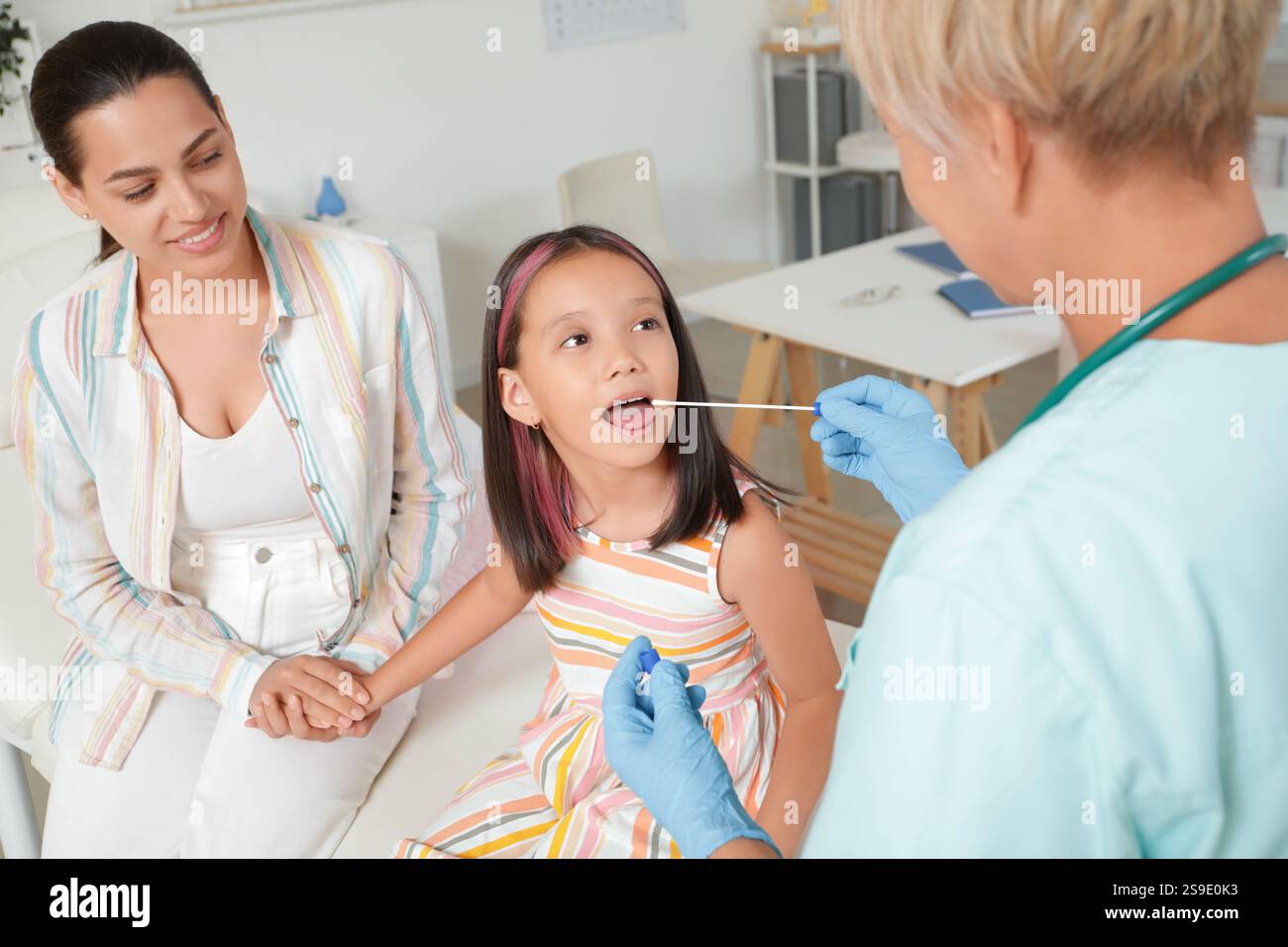 Female pediatrician taking sample from little girl's mouth and mother ...