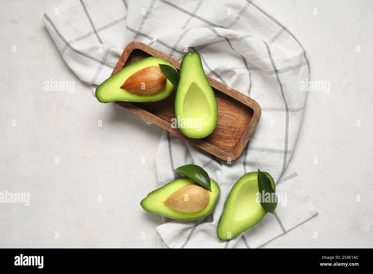 Wooden tray with halves of fresh ripe avocados on white background ...