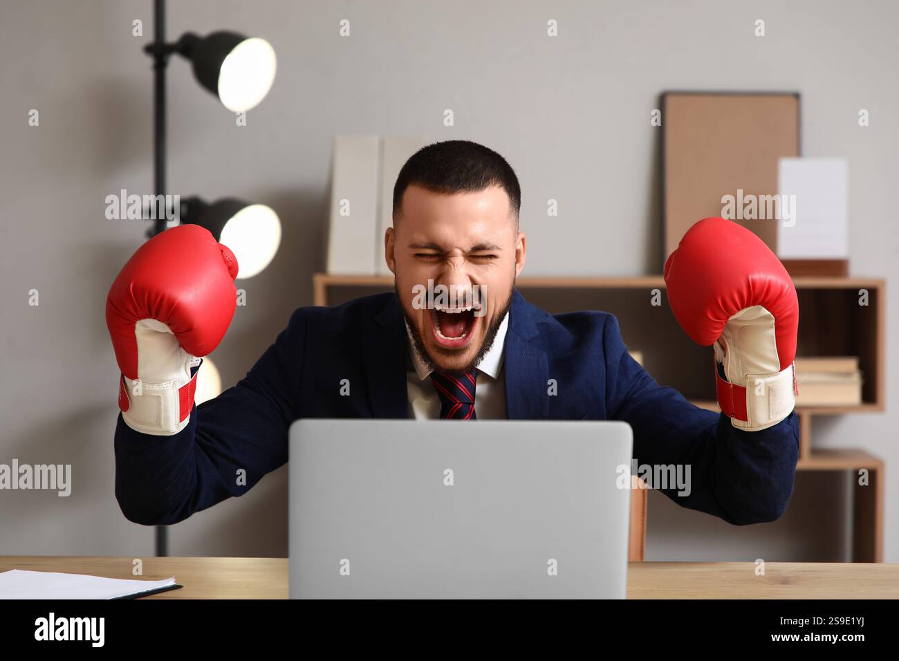 Angry businessman with boxing gloves and laptop at table in office ...