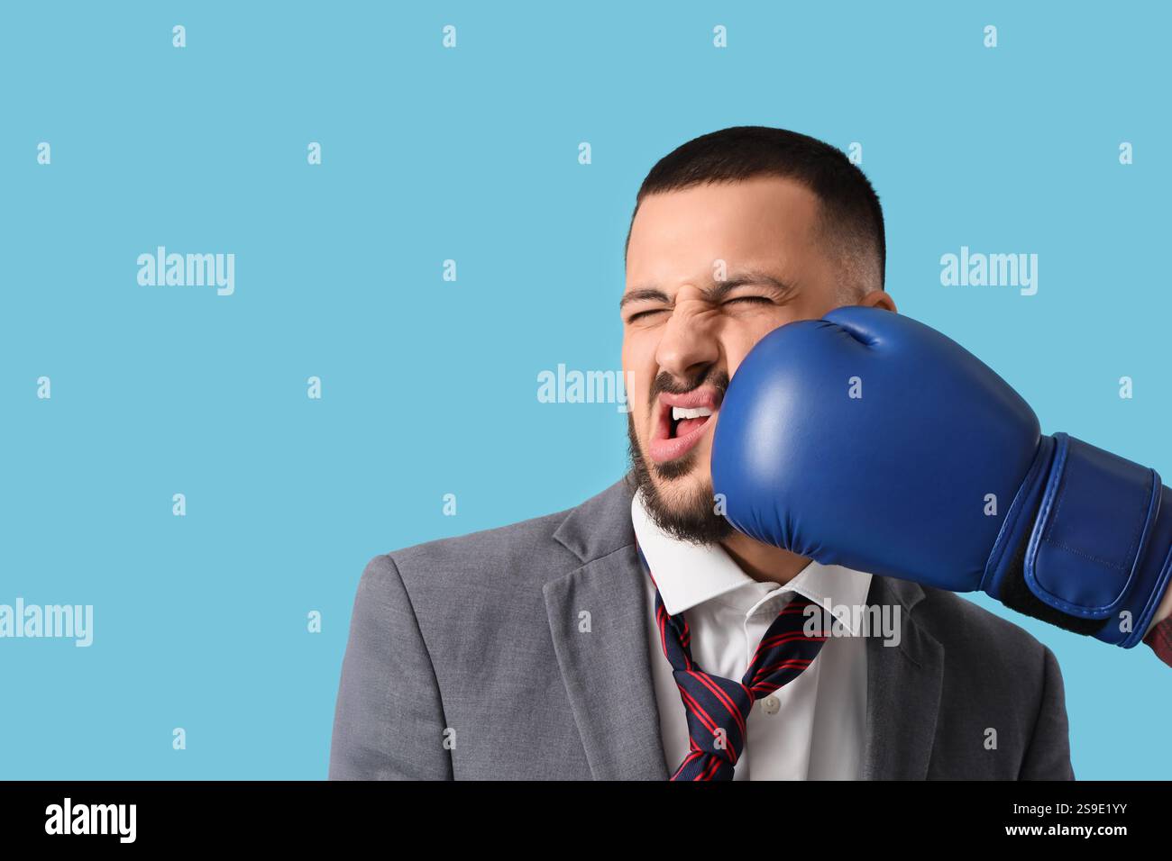 Young businessman getting hit in his face with boxing glove on blue ...