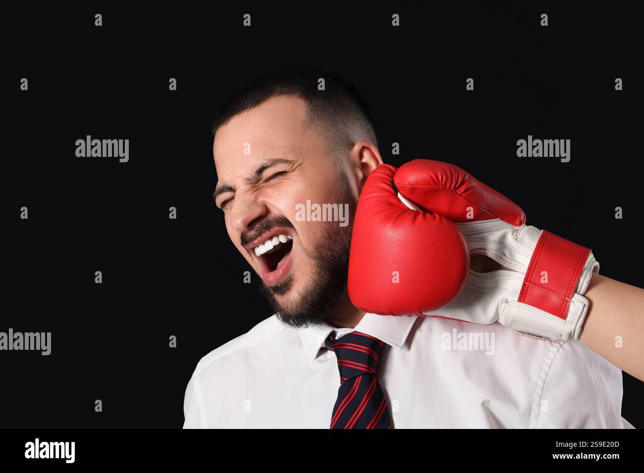 Young businessman getting hit in his face with boxing glove on black ...