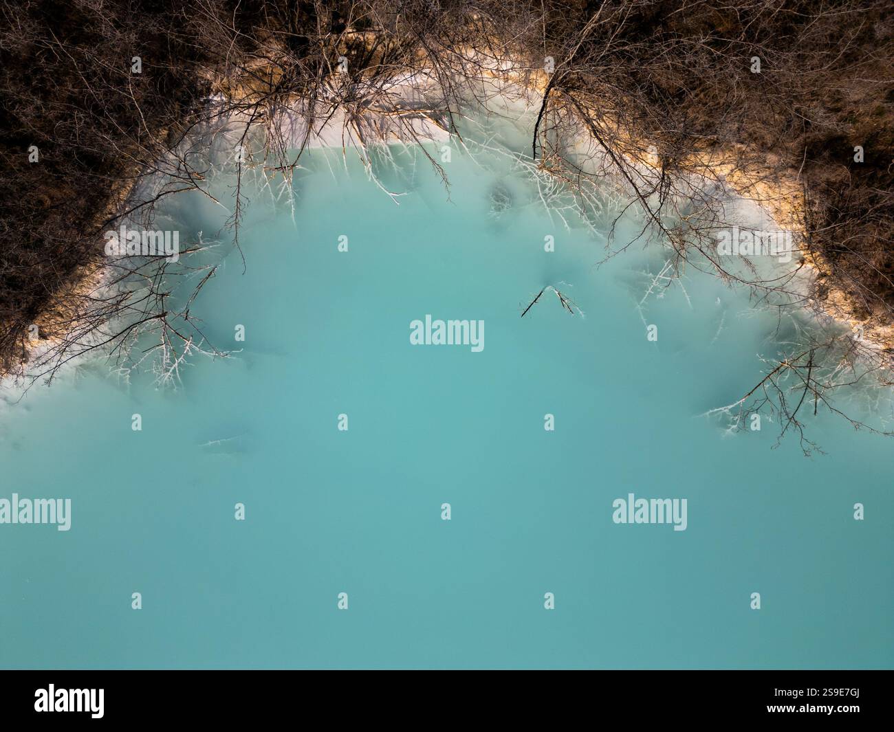 A turquoise tailings pond near a cement factory, surrounded by rugged ...
