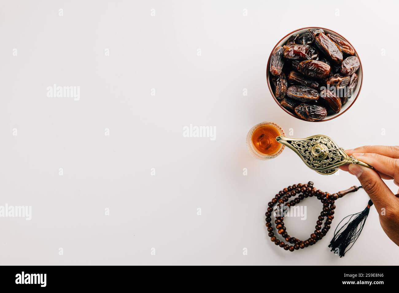 Hand pouring tea from a teapot with dates and prayer beads on white ...