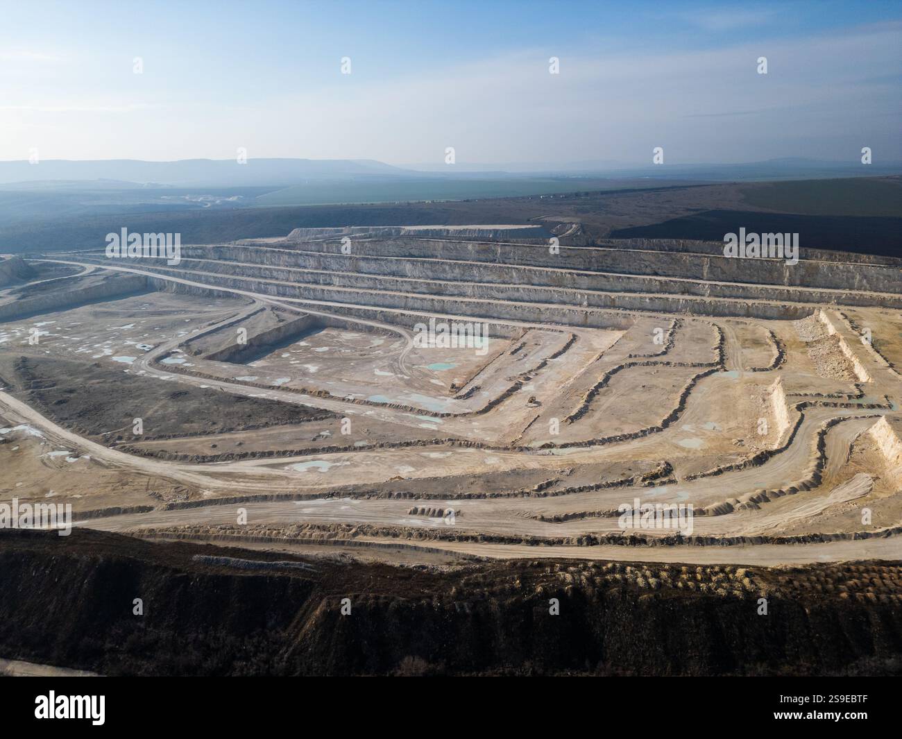 An open-pit quarry with terraced layers and heavy machinery operating ...