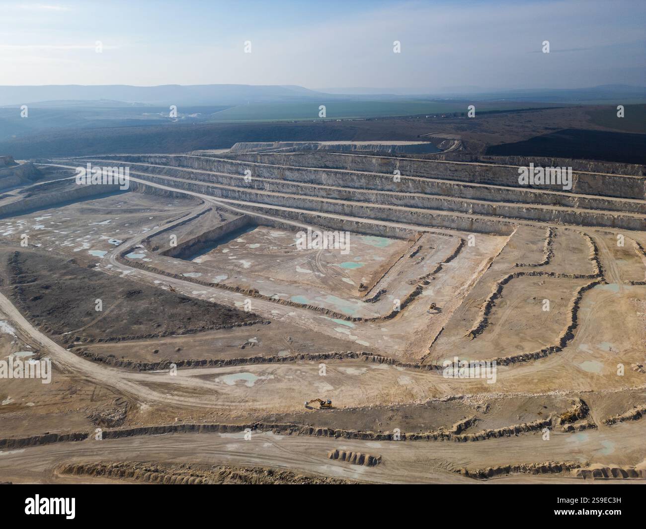 An open-pit quarry with terraced layers and heavy machinery operating ...