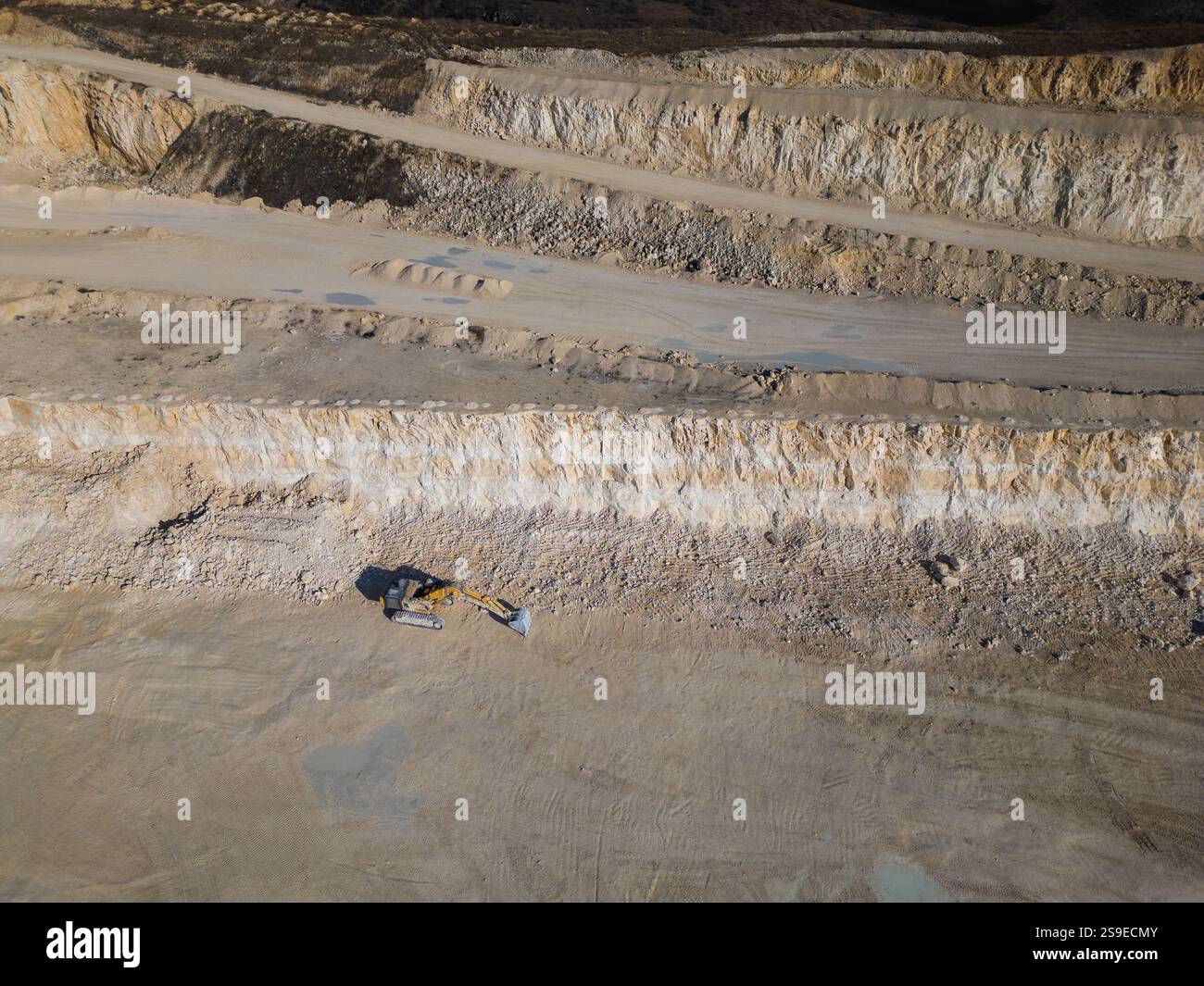 An open-pit quarry with terraced layers and heavy machinery operating ...