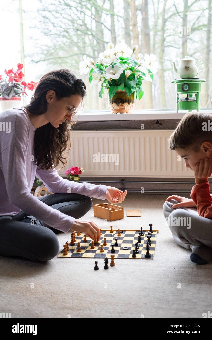 Mother and son concentrating while playing chess on the floor at home ...
