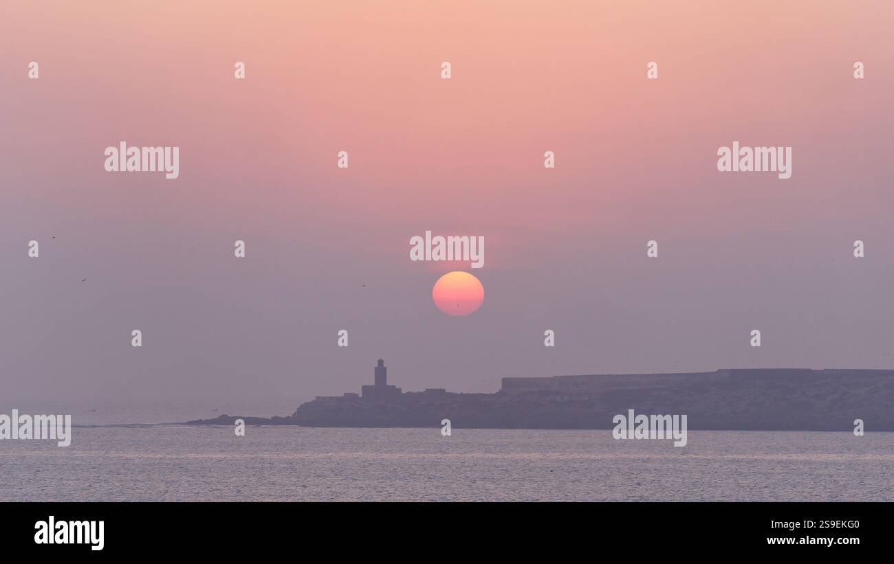 Sun sets above an Island on the horizon in the town of Essaouira ...