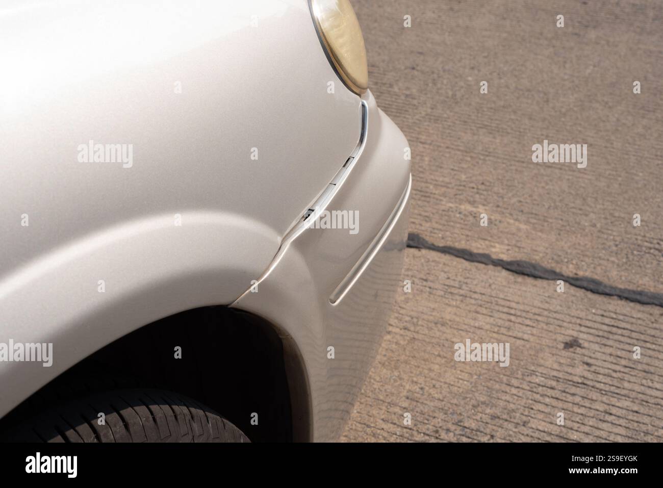 A close-up image of a silver car's front bumper showing visible damage ...