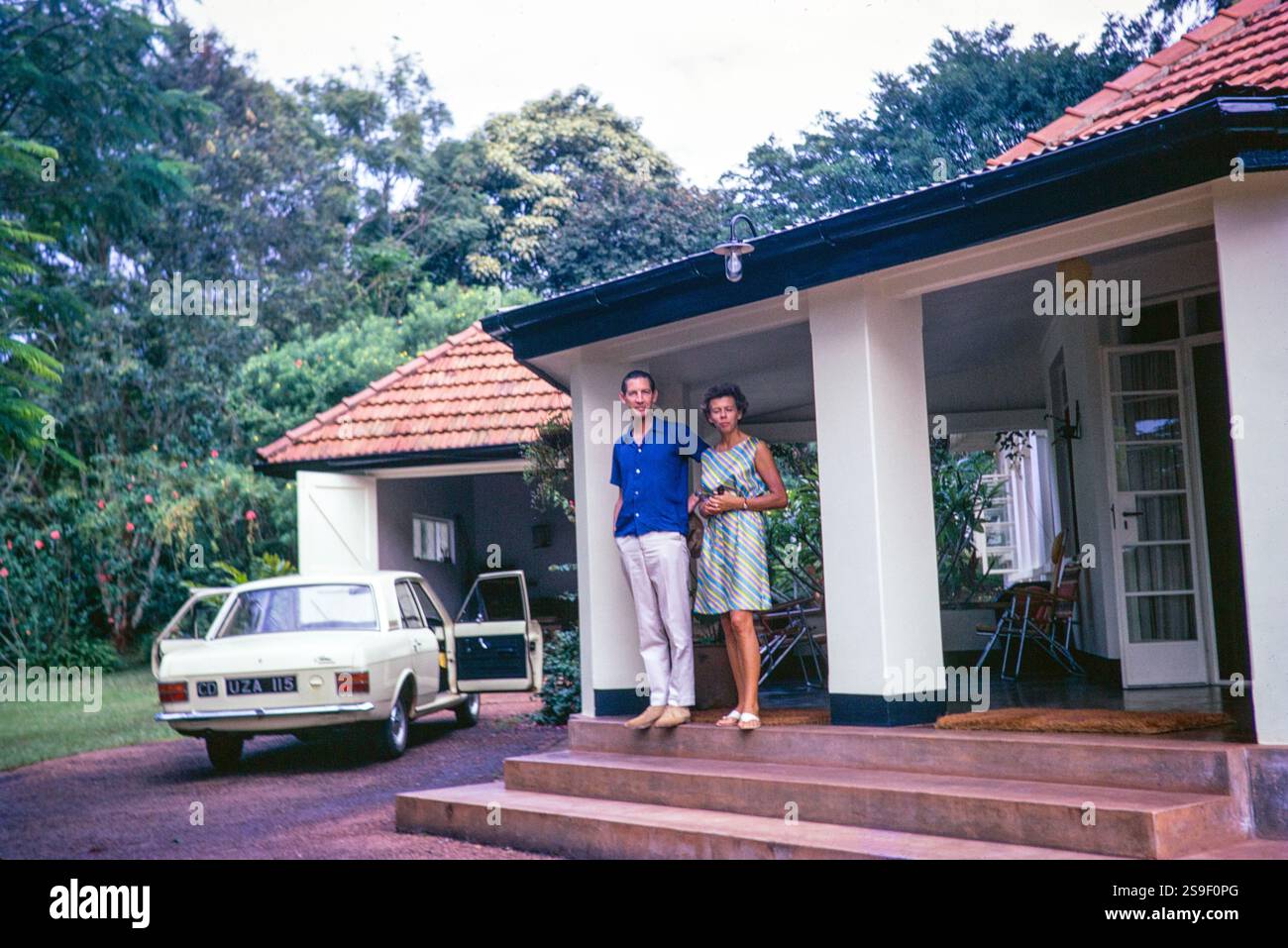 Man and woman stand at front of suburban house, car with CD suffix ...