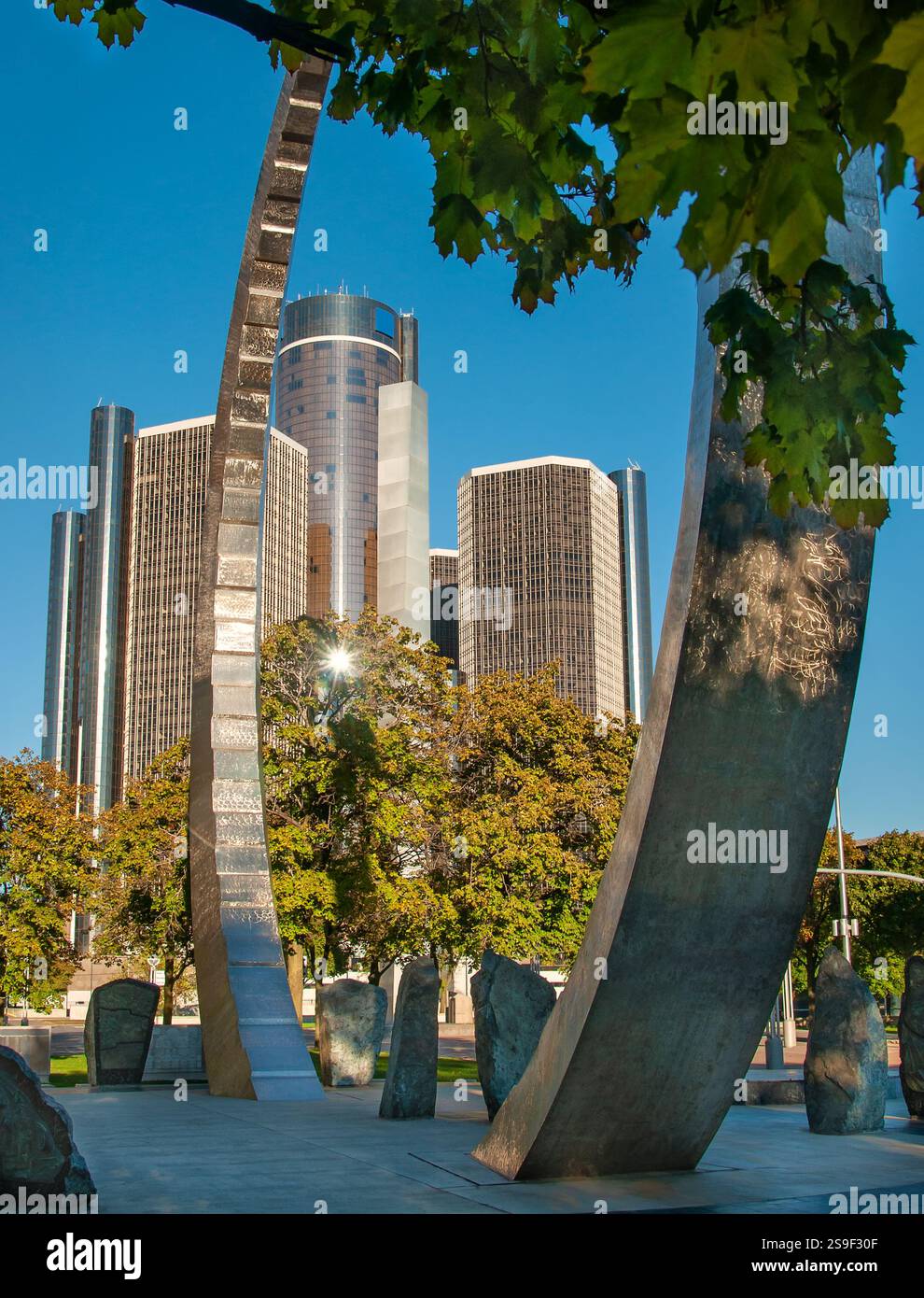 A metallic sculpture in a park with modern skyscrapers rising in the ...